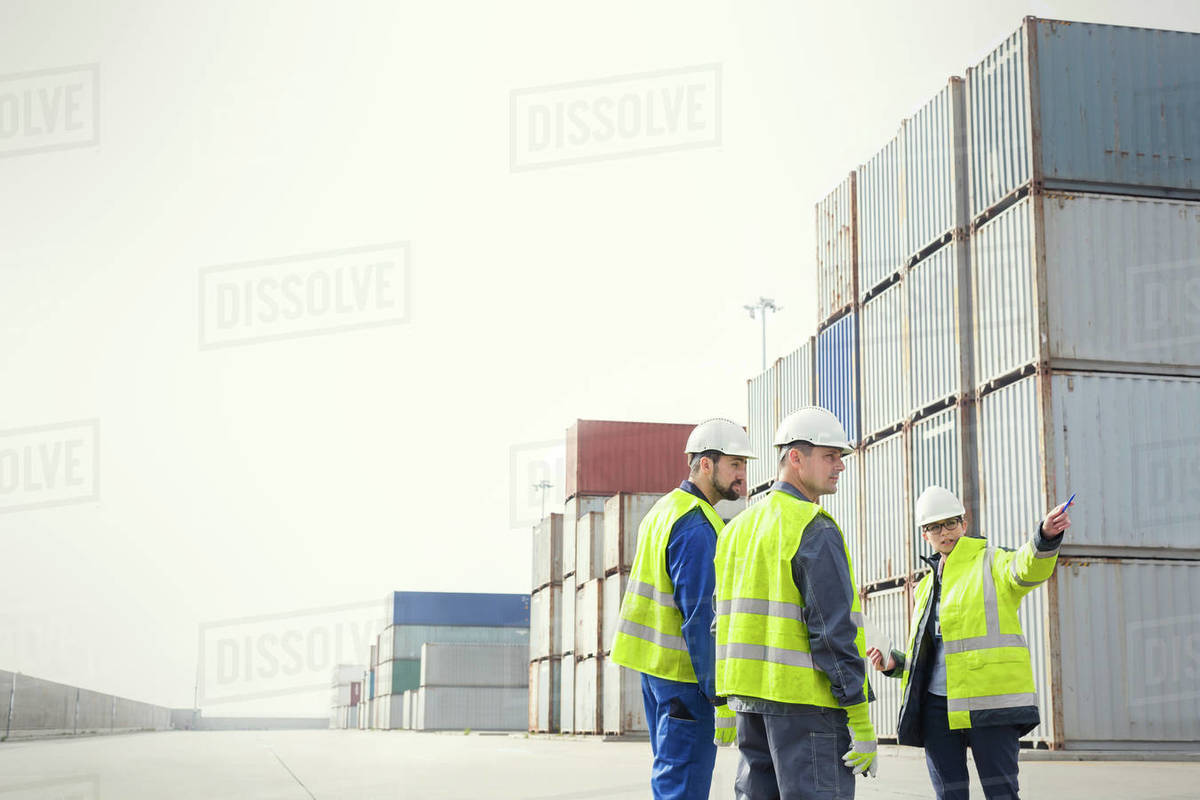 Dock workers and manager talking at cargo containers at shipyard ...