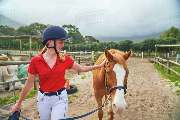 Teenage girl in equestrian helmet leading horse along paddock - Stock ...