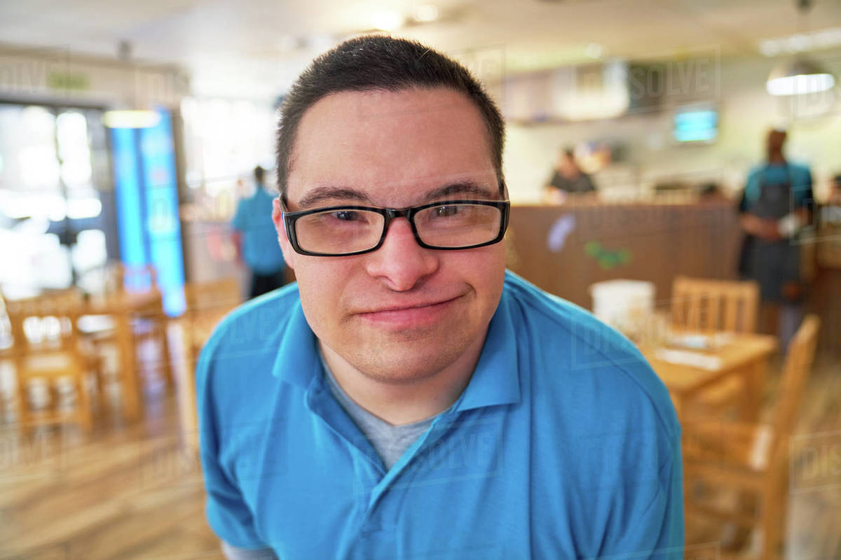 Close up portrait smiling young man with Down Syndrome in cafe ...