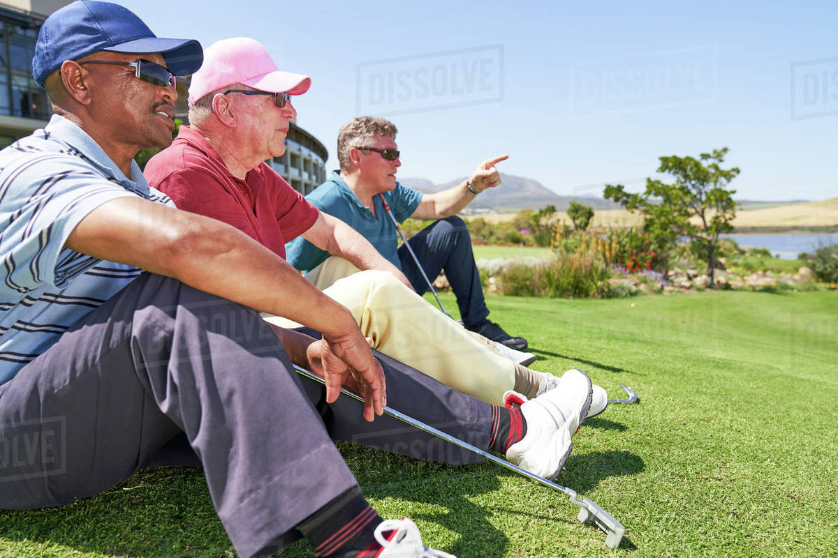 Male golfers resting sitting in grass on sunny golf course - Royalty ...