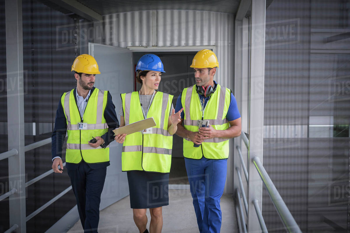 Supervisors with clipboard walking and talking on factory walkway ...