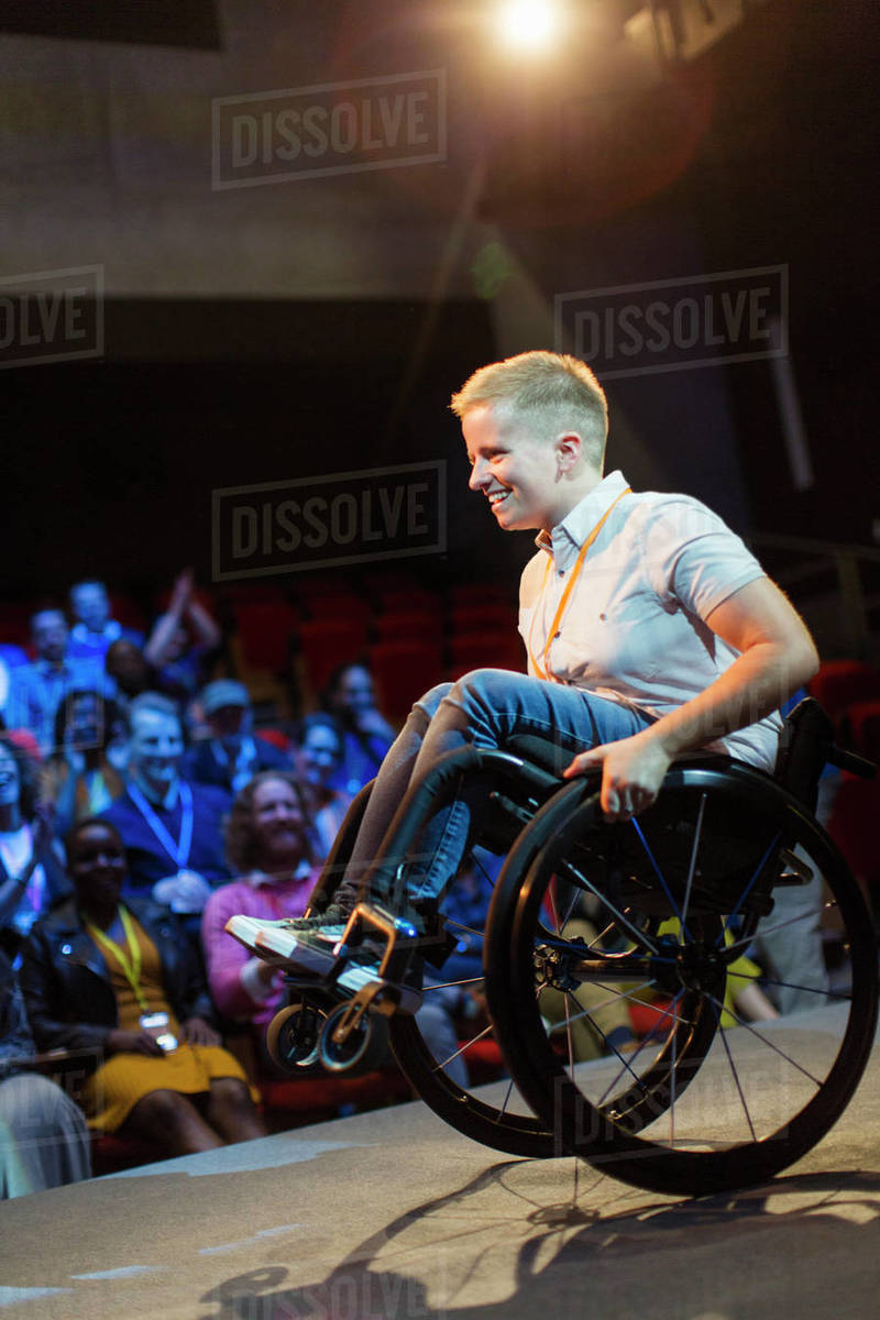 Smiling female speaker doing a wheelie in wheelchair on stage - Royalty ...