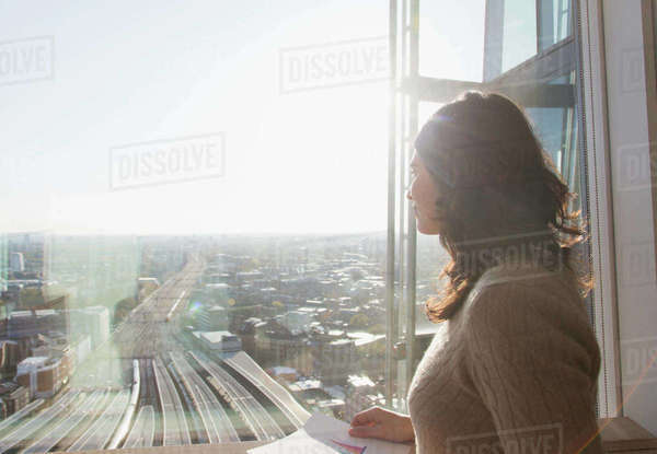 Thoughtful businesswoman at sunny window overlooking city - Stock Photo ...