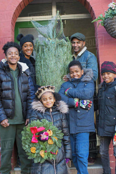 Portrait happy family with Christmas tree and wreath on front stoop ...
