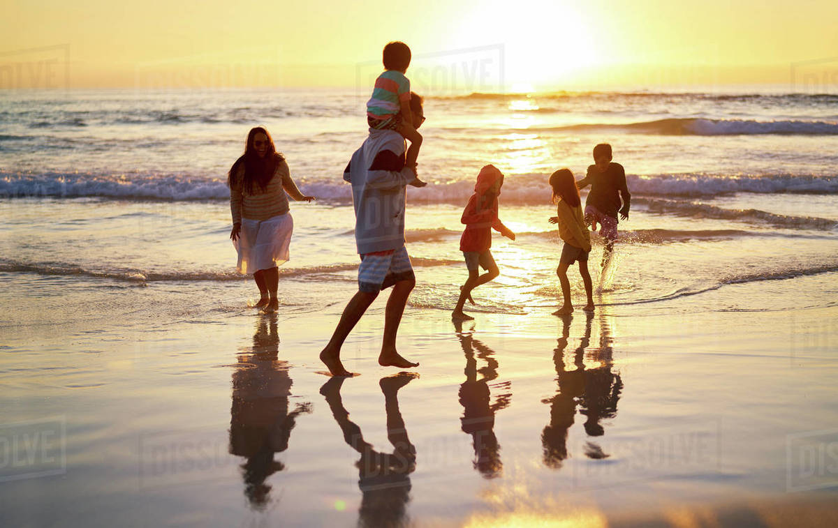 Family wading in surf on idyllic ocean beach at sunset - Royalty-free ...