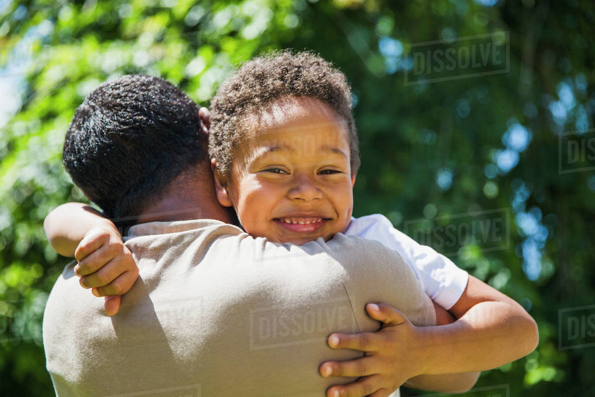 Portrait happy son hugging father in sunshine - Stock Photo - Dissolve