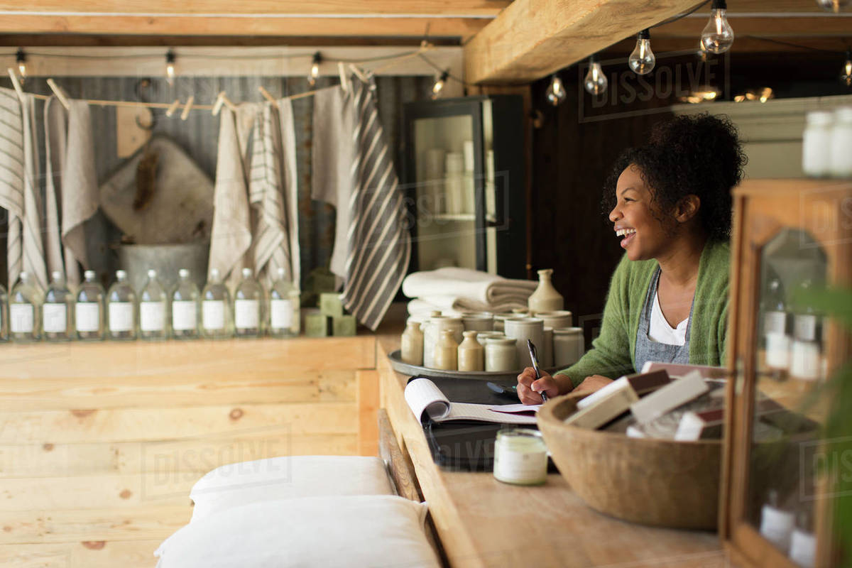 Happy female shop owner laughing at shop counter - Stock Photo - Dissolve