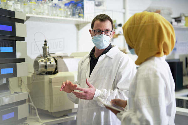 Scientists in face masks talking in laboratory - Stock Photo - Dissolve