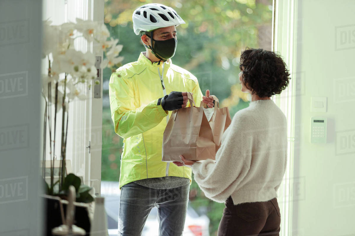 Woman receiving food delivery from man in face mask and helmet ...