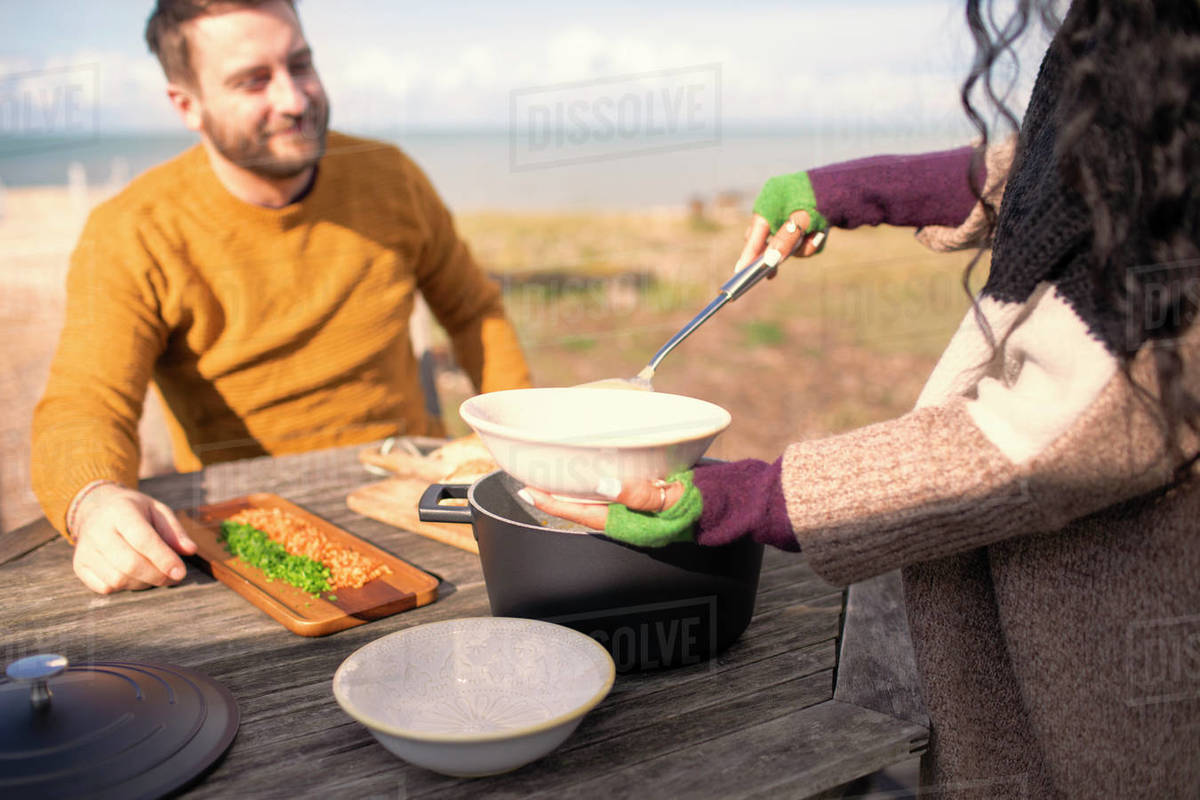 Woman serving chowder to boyfriend on sunny beach patio - Royalty-free ...