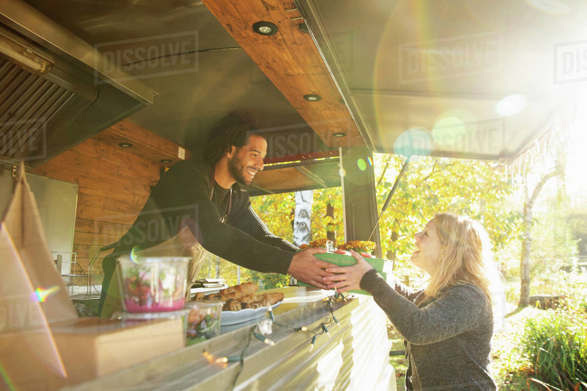 Happy food truck owner serving food to customer in sunny park - Royalty ...