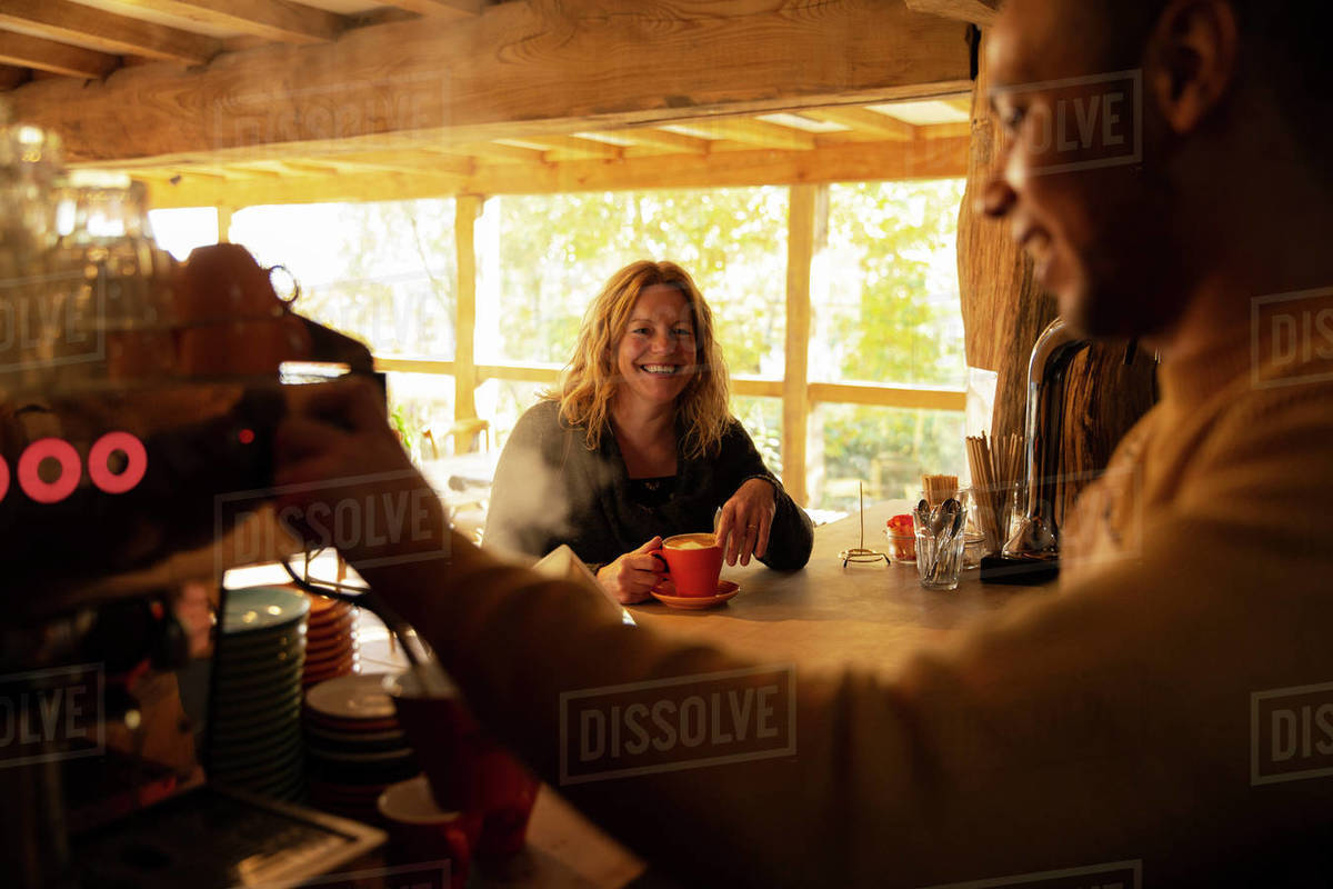 Customer watching barista prepare coffee at espresso machine in cafe ...