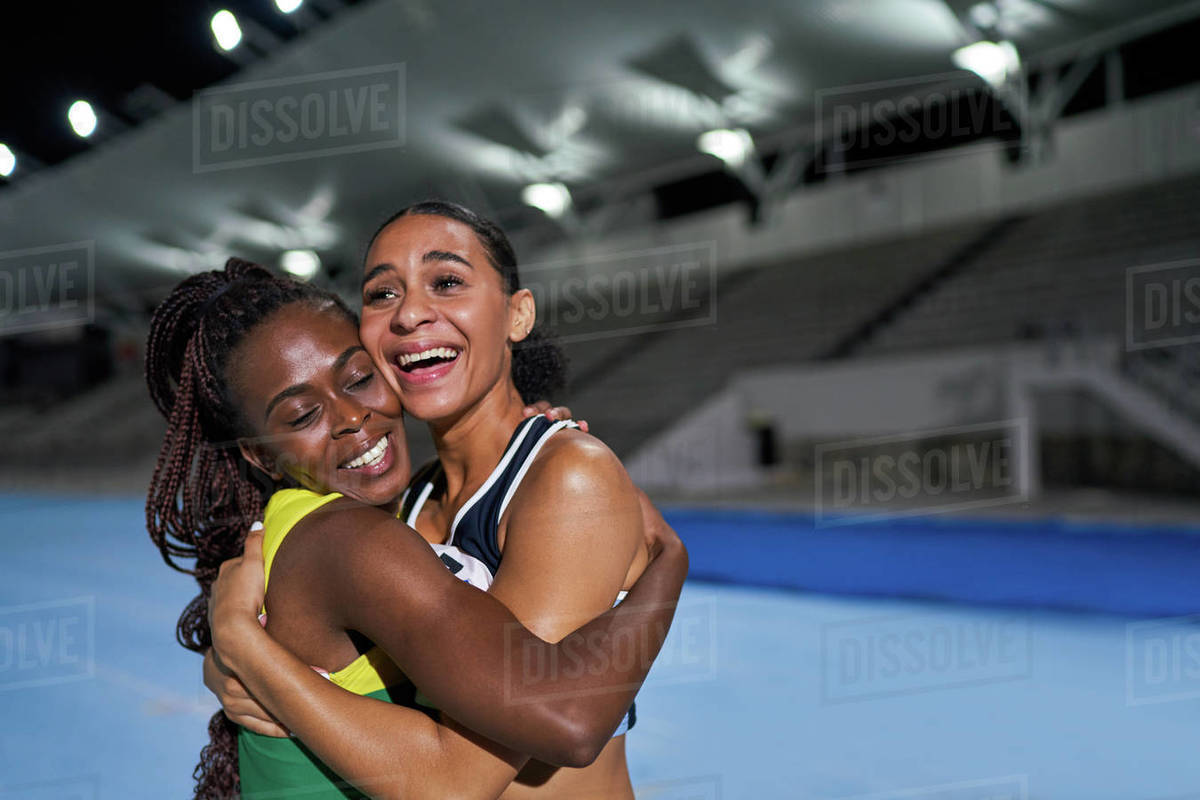 Happy female track and field athletes hugging on track at night ...