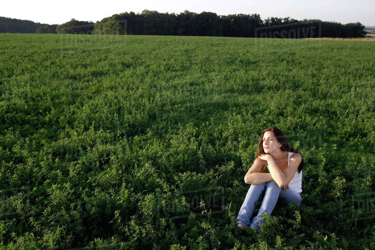 Young woman sitting in field - Royalty-free Stock Photo | Dissolve