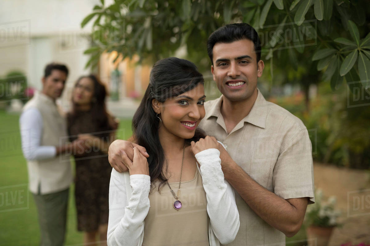 Man with hands on woman's shoulder with friends in background - Stock ...