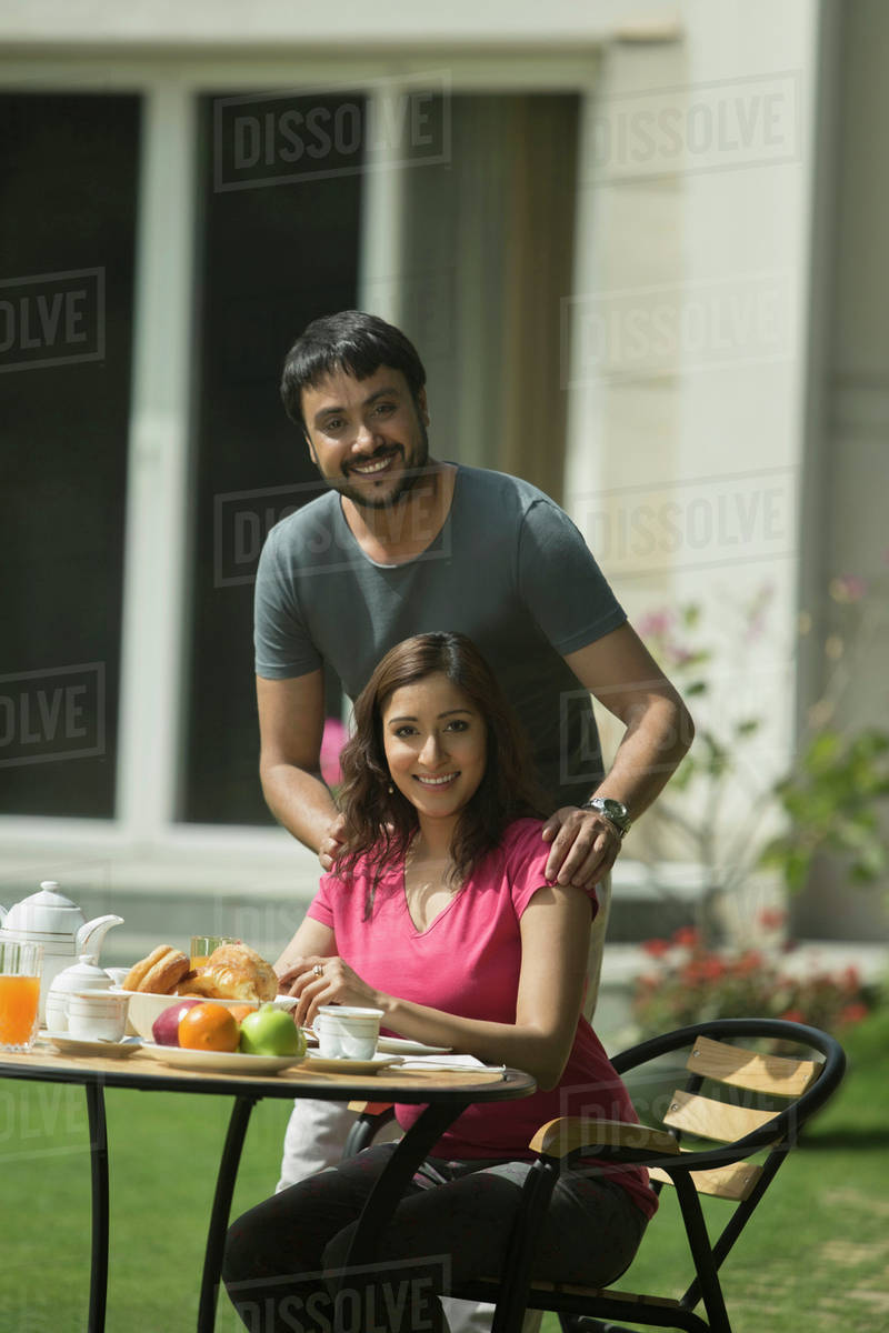 Man standing behind woman, at breakfast table outside - Royalty-free ...