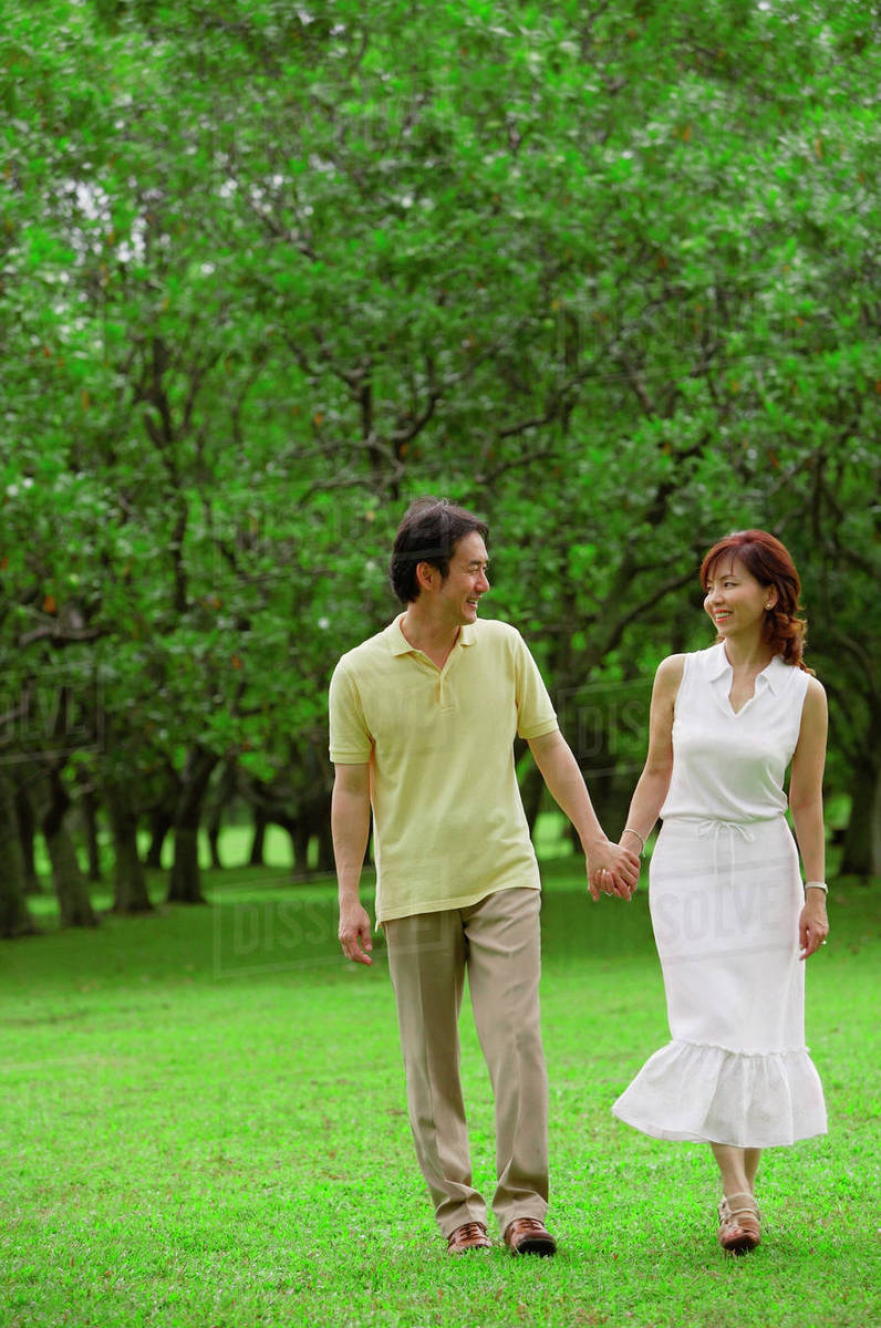 Couple walking side by side in park, holding hands - Stock Photo - Dissolve