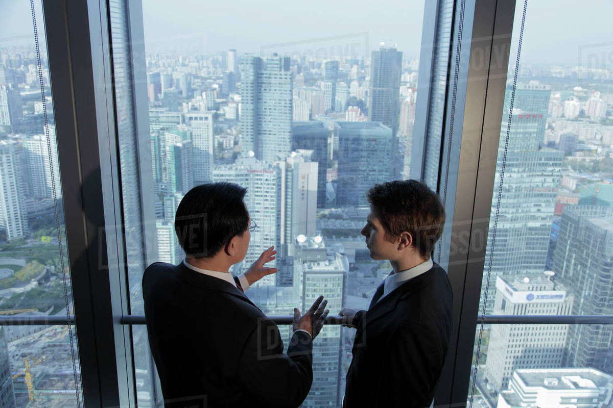 Two men talking in front of window with a view of the city of Beijing ...