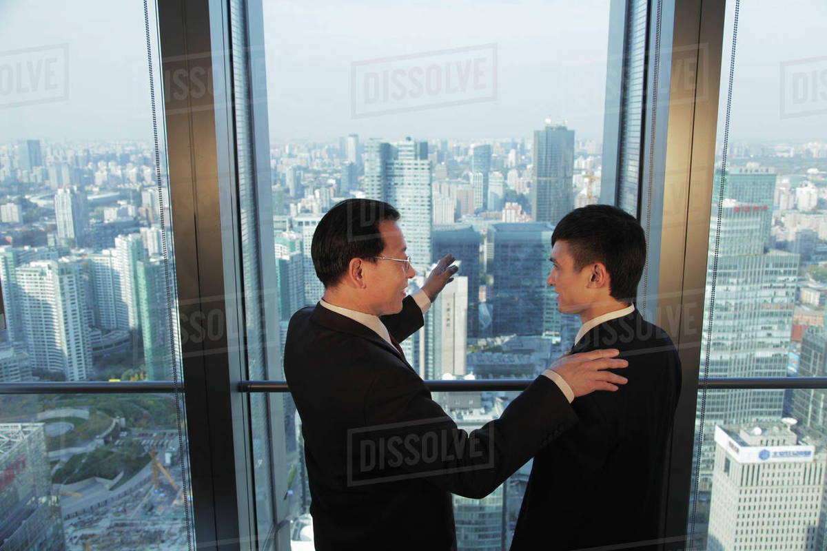 Two men talking in front of window with a view of the city of Beijing ...