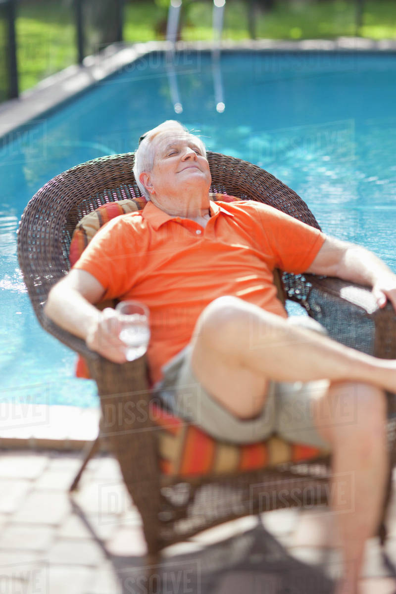 A retired senior man relaxing in the sun next to a pool - Royalty-free ...