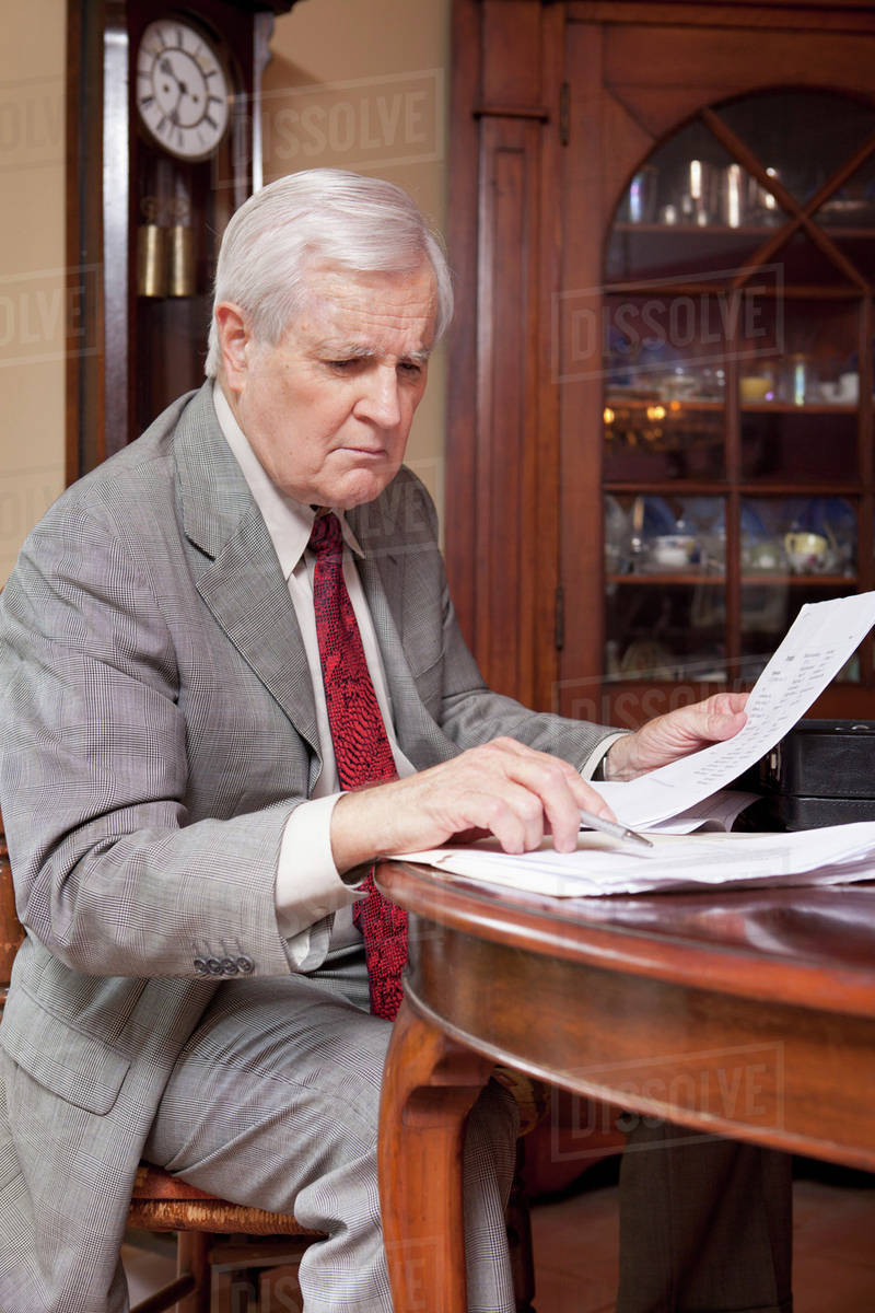 A businessman considering some paperwork at home - Stock Photo - Dissolve