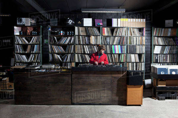 A young man using decks and a sound mixer at a record store - Stock ...