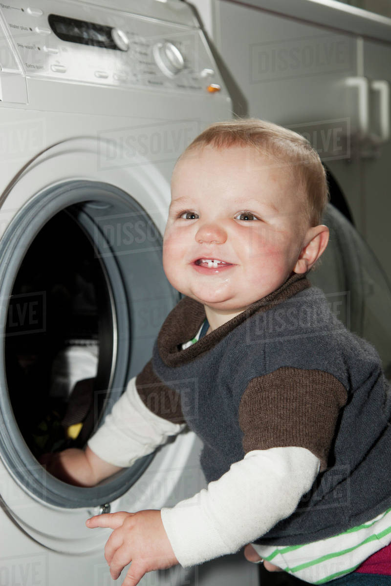 A baby boy standing next to a washing machine - Stock Photo - Dissolve