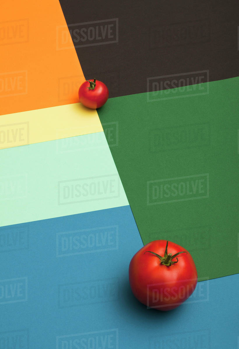 A large tomato and a small tomato placed on a multi colored geometric ...