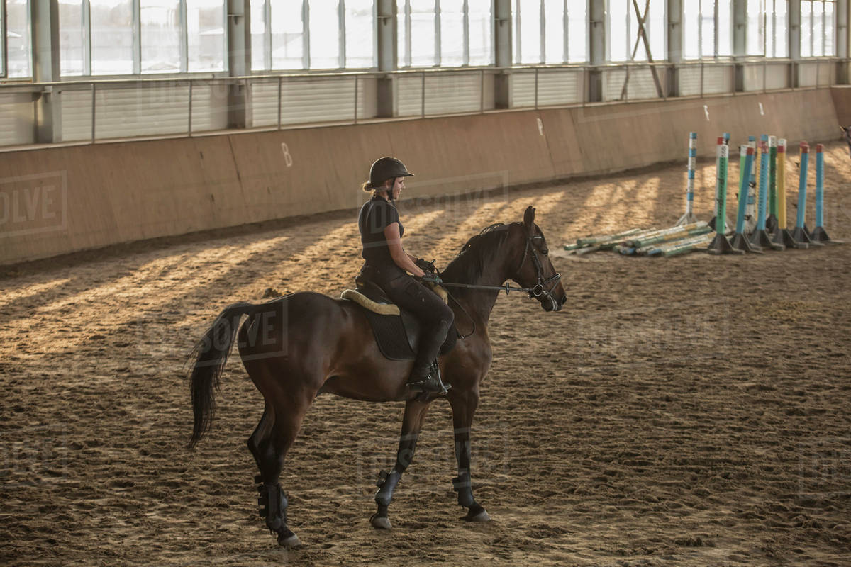 Side view of woman riding horse in training stable - Stock Photo - Dissolve