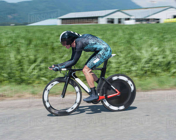 Full length side view of cyclist riding bicycle on country road against ...