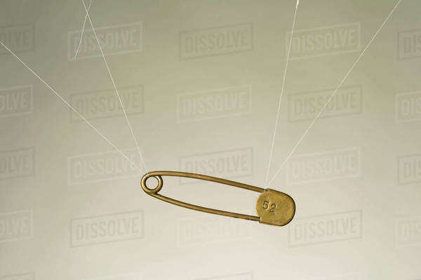 Strings tied to safety pin hanging against white background - Stock ...