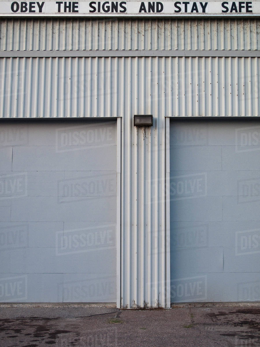 A sign reading OBEY THE SIGNS AND STAY SAFE atop a warehouse building ...