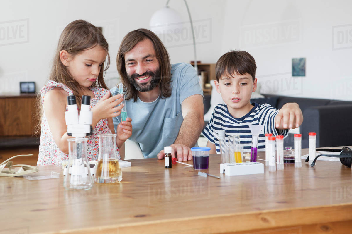 Father and children doing science experiment on table in house ...
