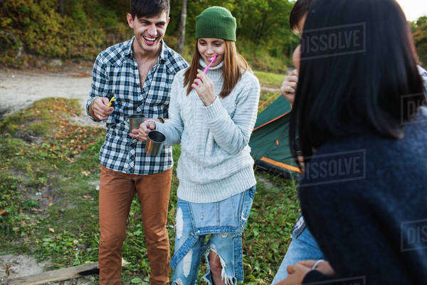 Happy friends brushing teeth at campsite - Stock Photo - Dissolve