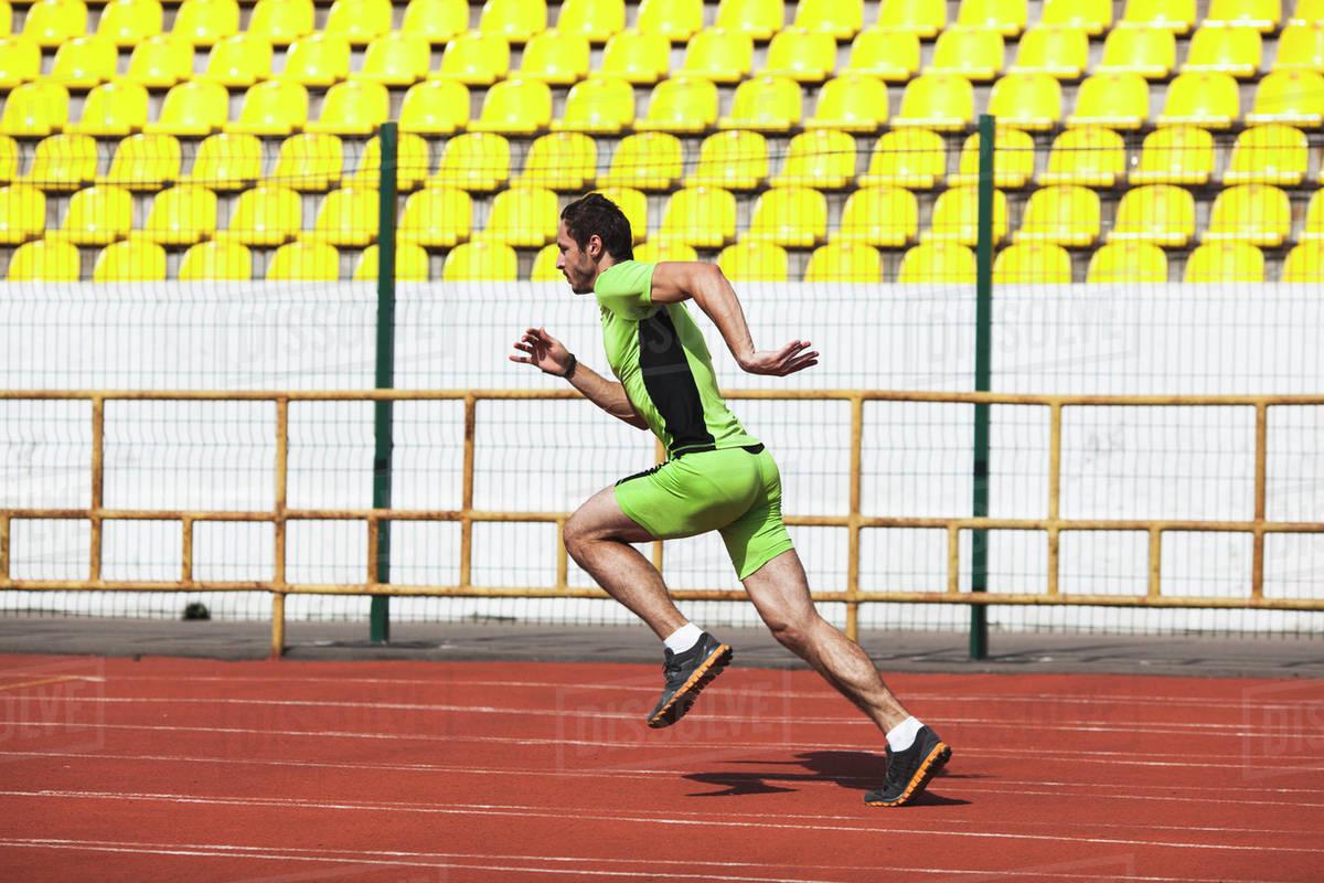 Full length side view of sporty young man running on race track in ...