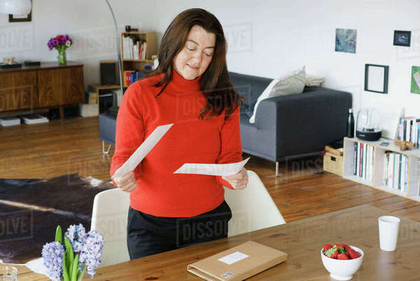 Mature woman holding letters while standing by table at home - Royalty ...