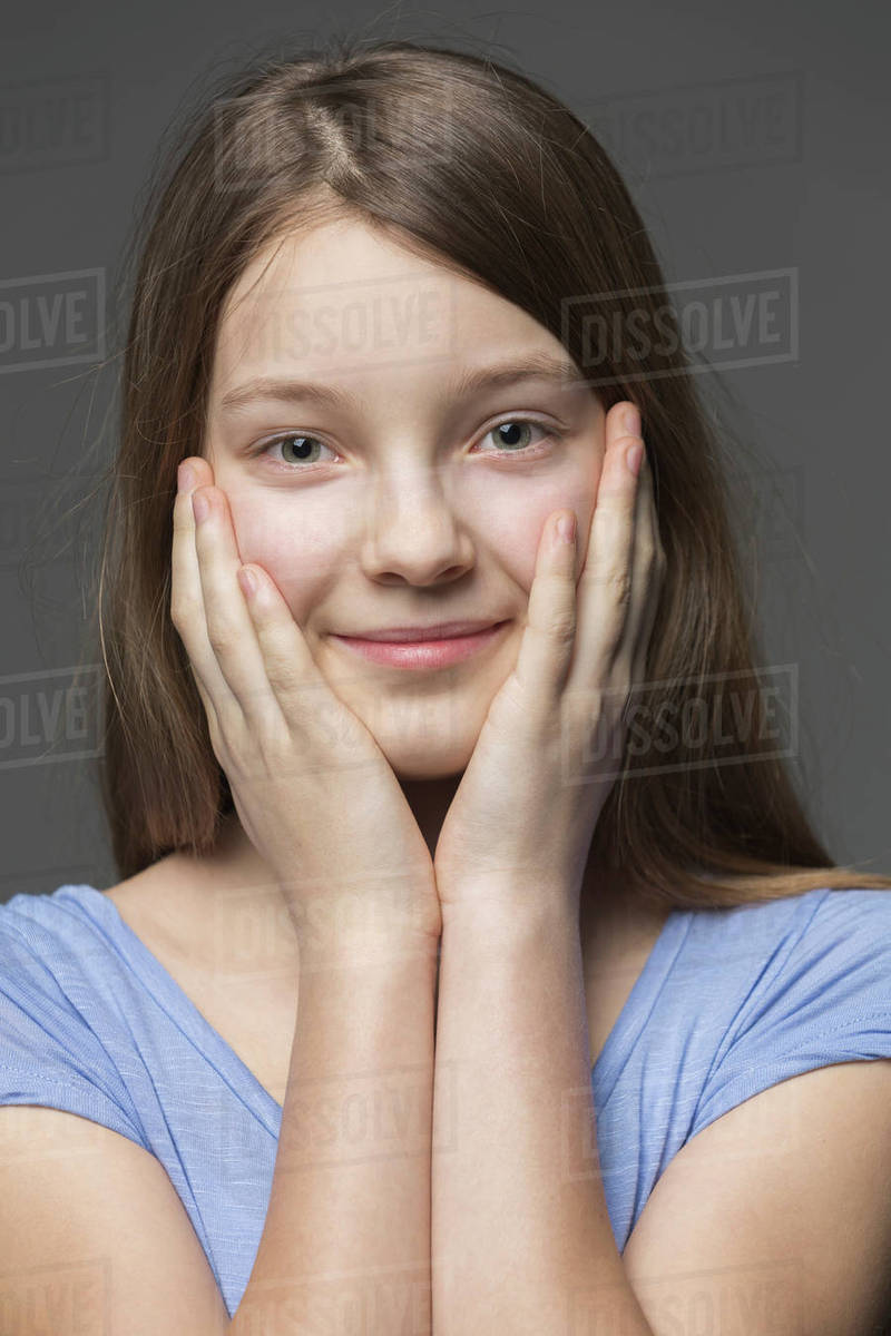 Close-up portrait of smiling girl with head in hands against gray ...