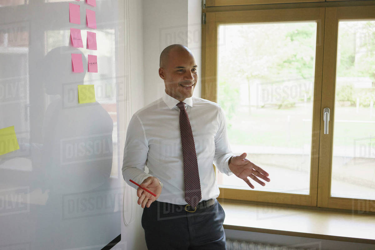 Confident businessman explaining in board meeting by whiteboard at ...