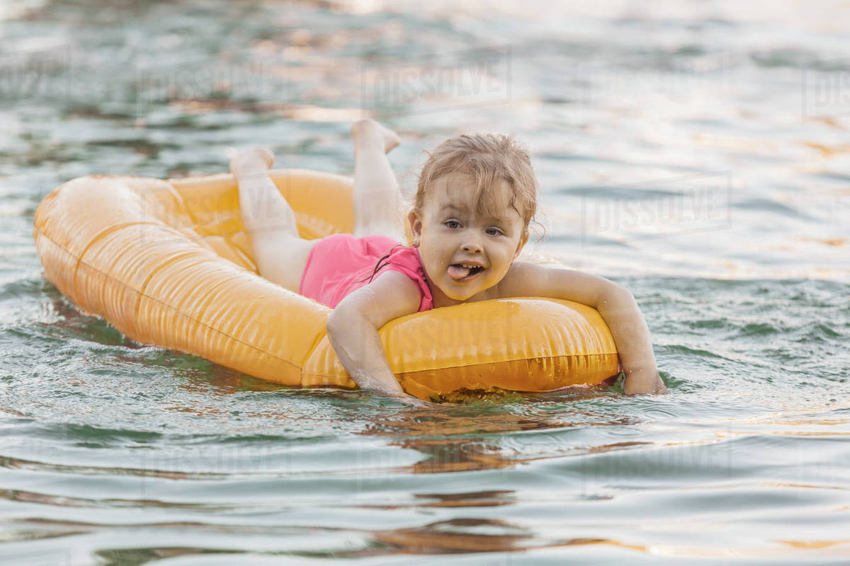 Cheerful cute girl floating on raft in lake - Stock Photo - Dissolve
