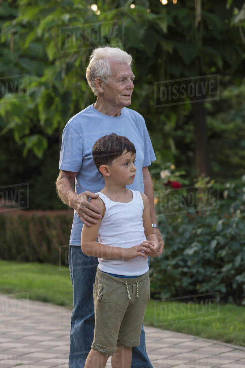 Smiling grandfather standing with grandson on footpath at park ...