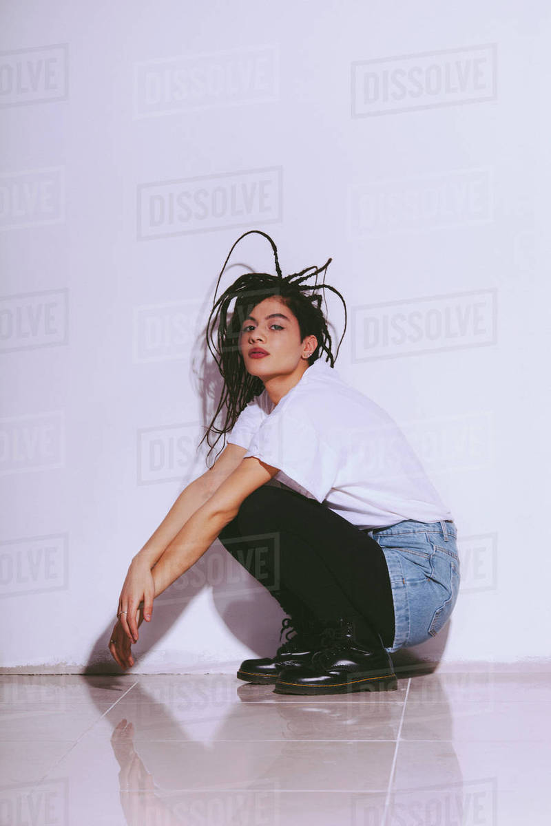 Portrait of fashion model crouching on tiled floor against white wall ...