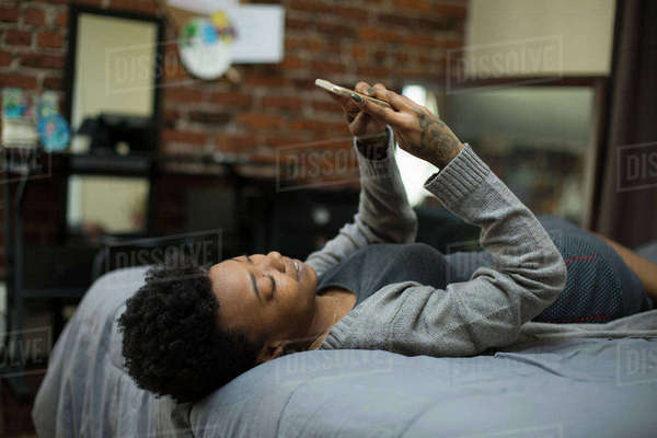 Young woman lying on bed using mobile phone at home - Royalty-free ...