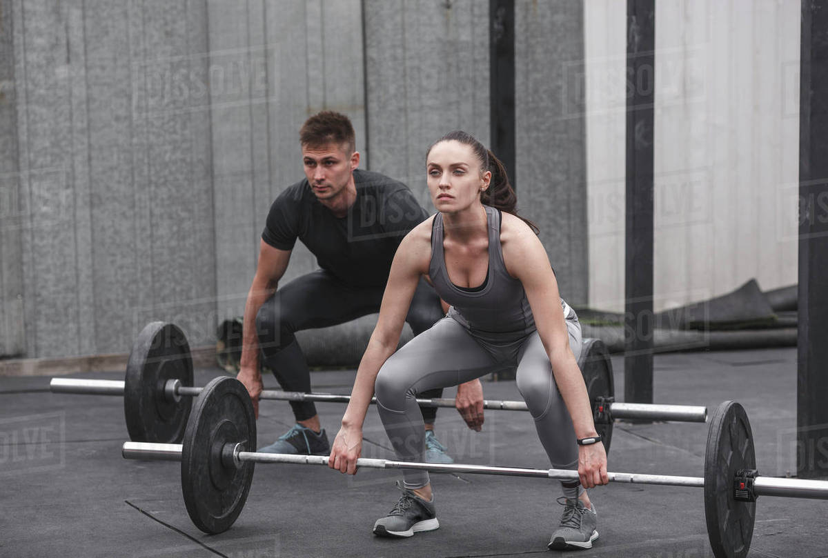 Full length of male and female athlete exercising with barbells during ...