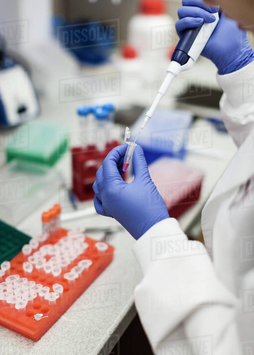 Scientist pouring chemical in vial through pipette at laboratory ...