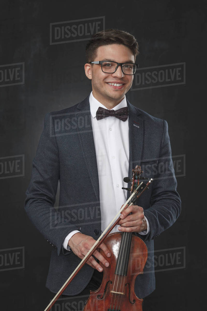 Portrait of smiling young man holding violin while standing against ...