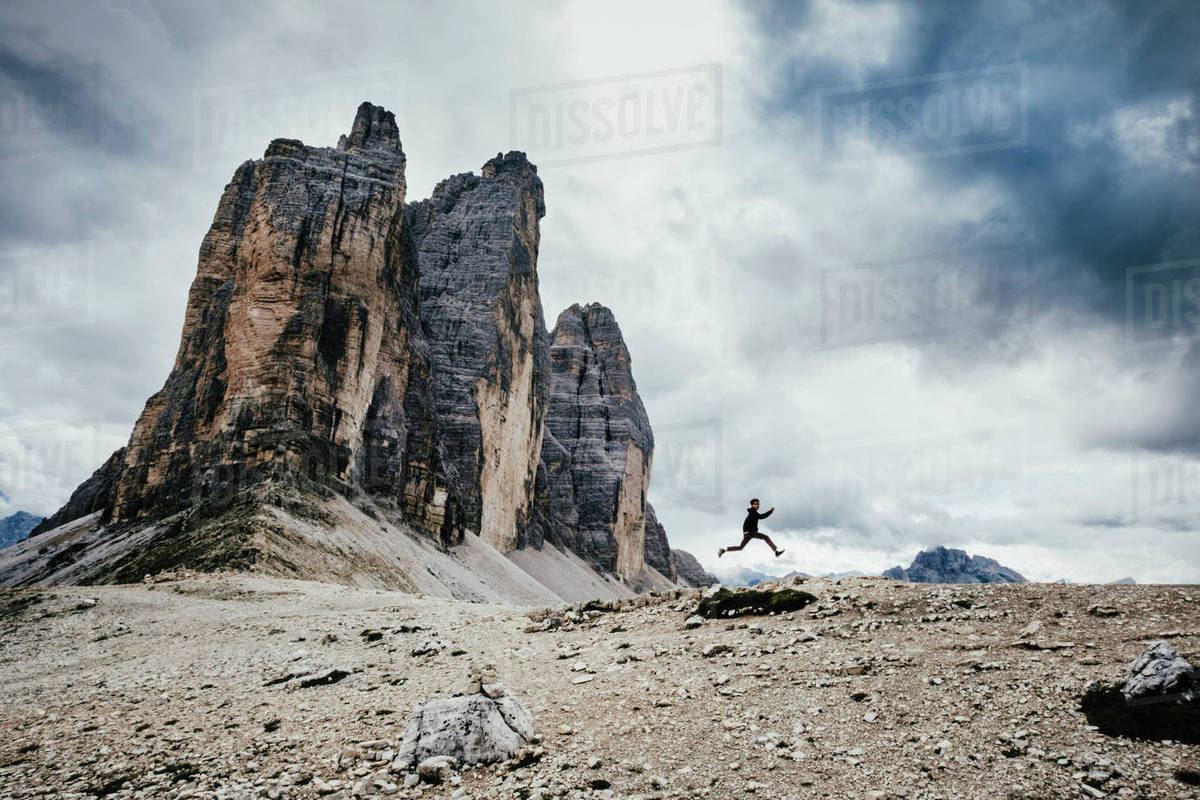 Low angle view of teenage boy jumping over rocks in alps against cloudy ...