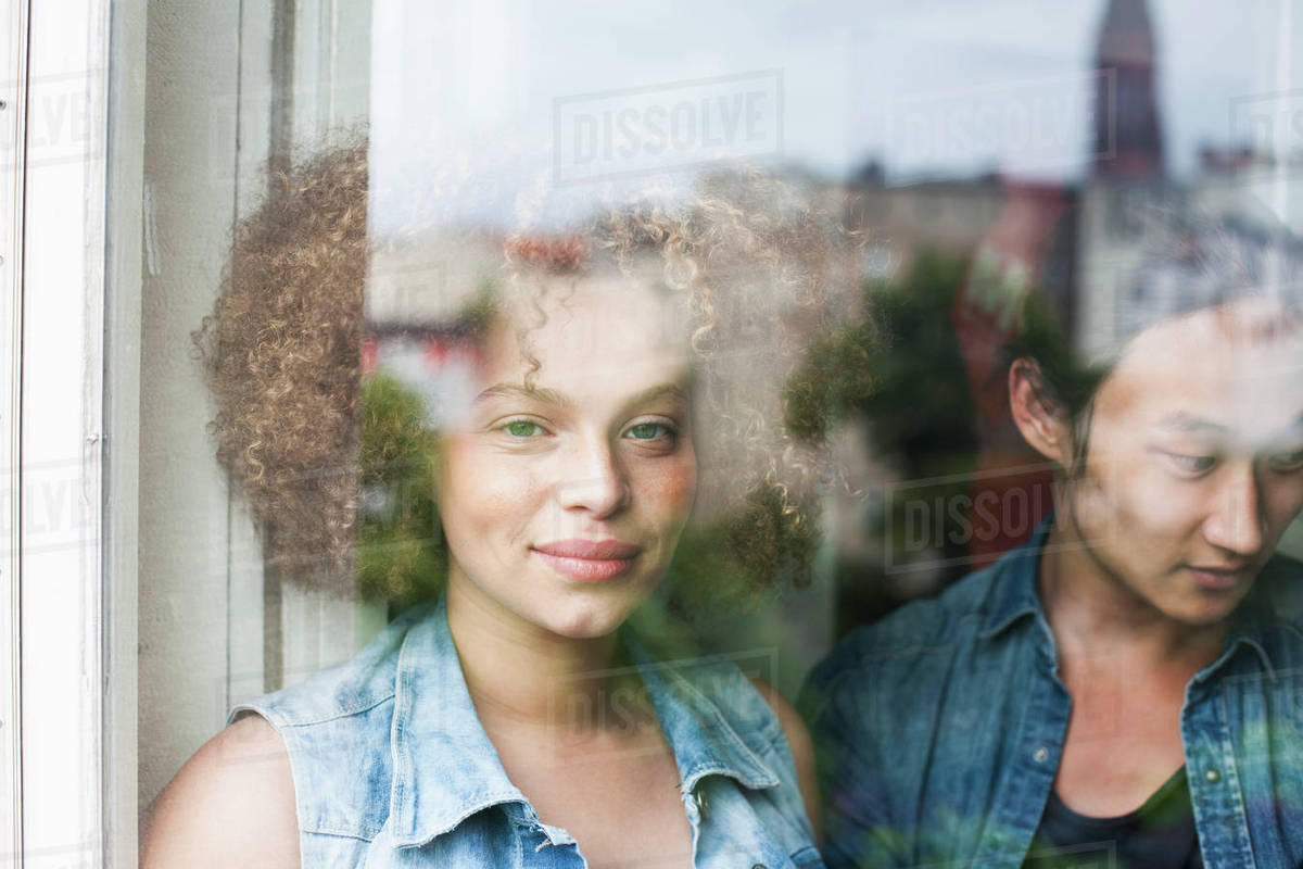 Portrait of smiling woman standing with man seen through glass window ...