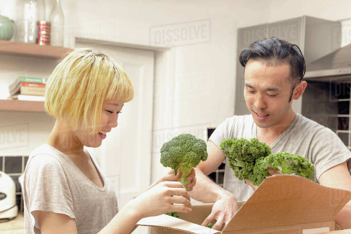 Smiling young couple removing fresh vegetables from cardboard box ...