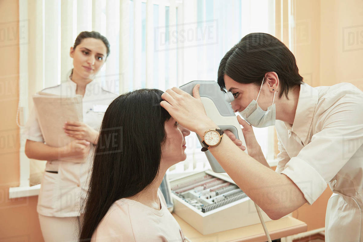 Nurse looking at optometrist examining female patient at hospital ...