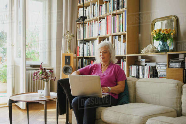 Senior woman using laptop on living room sofa - Stock Photo - Dissolve